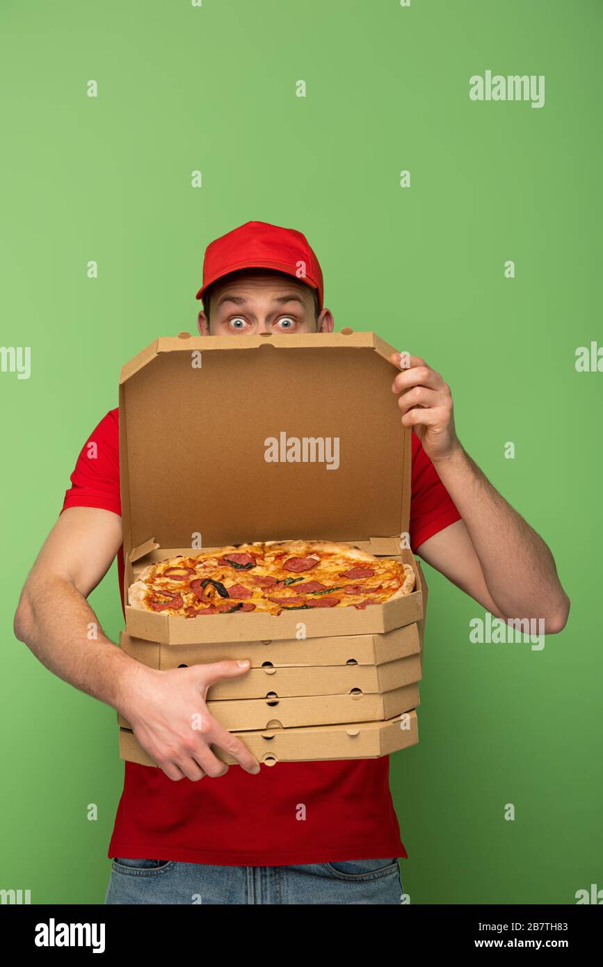 shocked delivery man in red uniform hiding behind pizza boxes on green ...