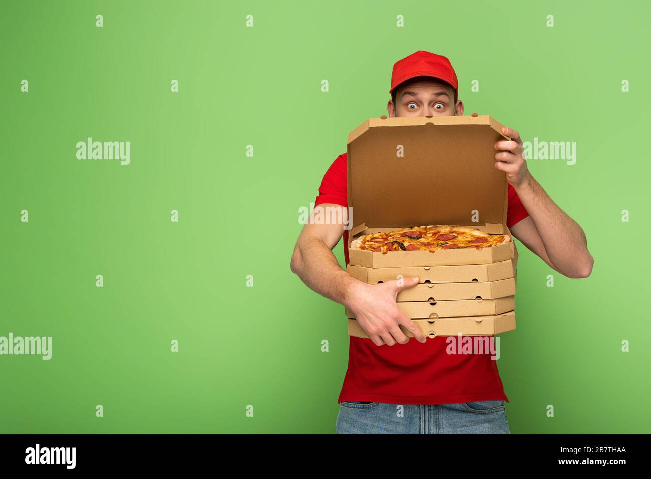 shocked delivery man in red uniform hiding behind pizza boxes on green ...