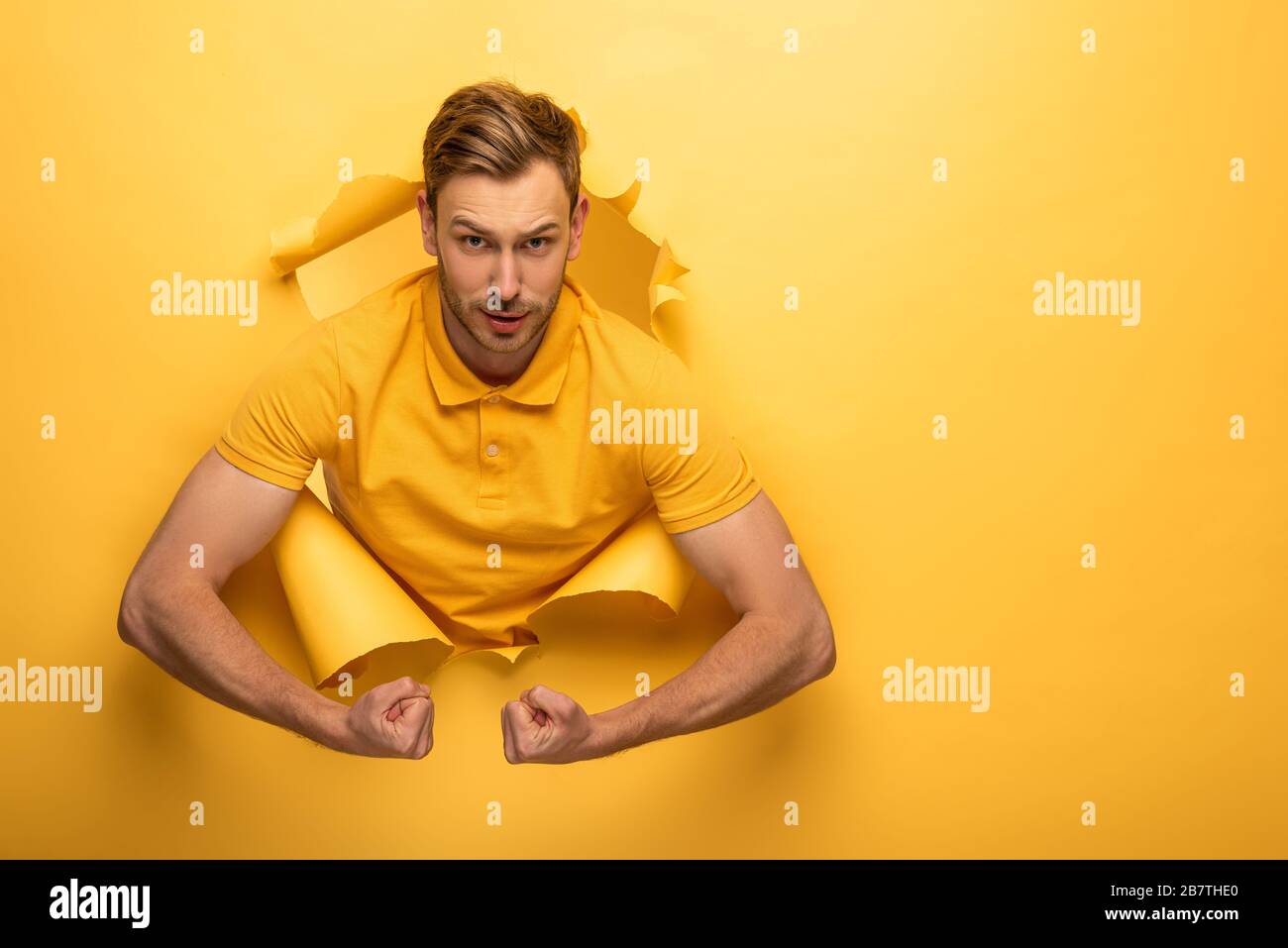strong handsome man in yellow outfit showing biceps in yellow paper ...