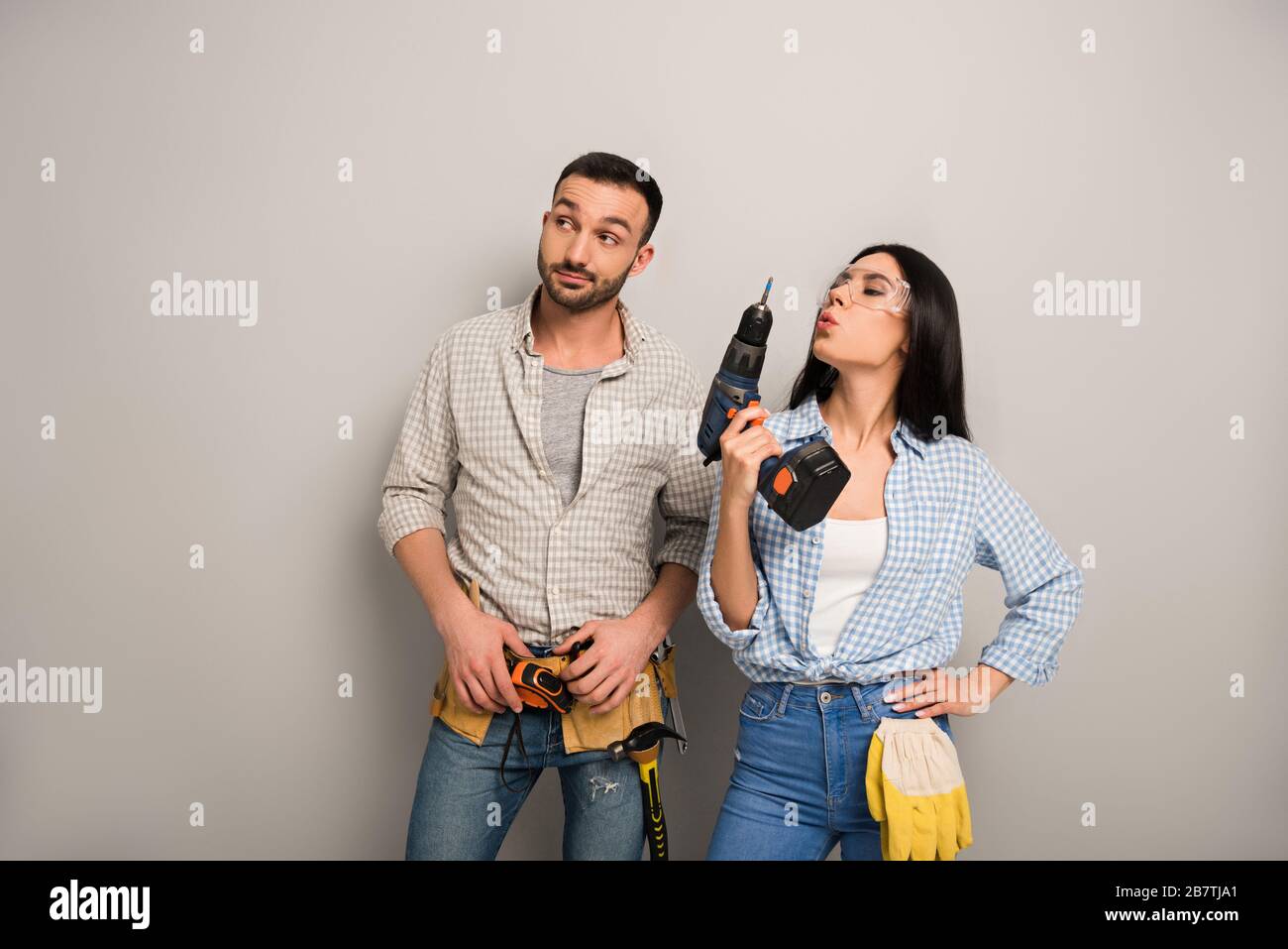 skeptical repairman and confident female worker holding electric drill ...