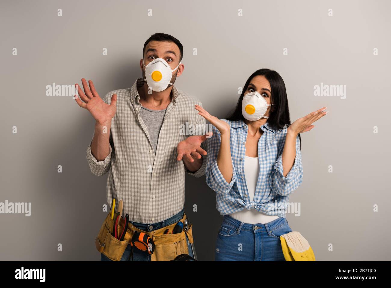 confused manual workers in safety masks with shrug gesture on grey ...
