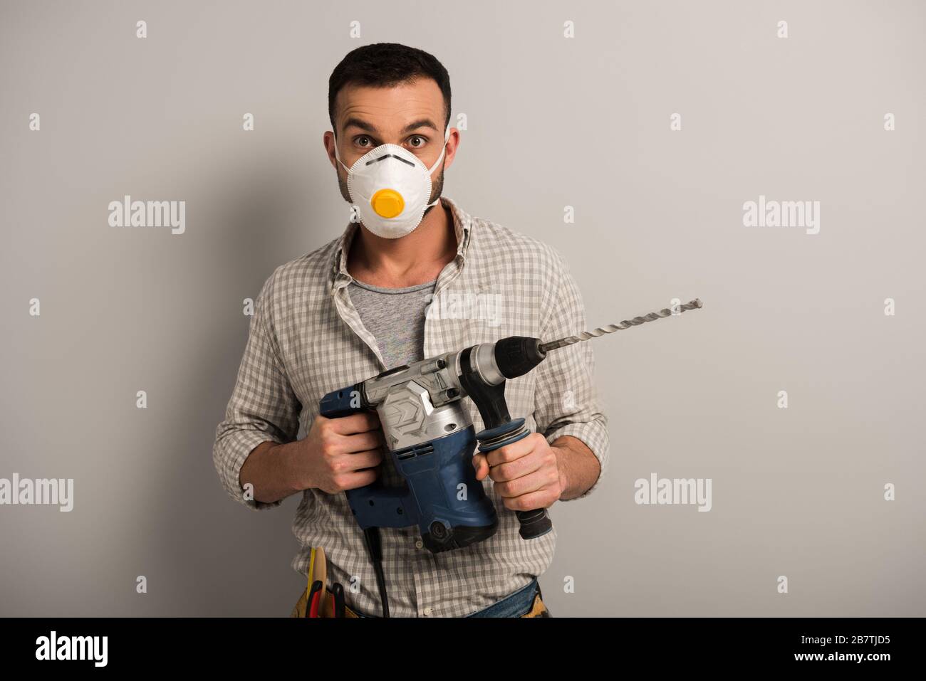 repairman in safety mask holding electric drill on grey Stock Photo - Alamy