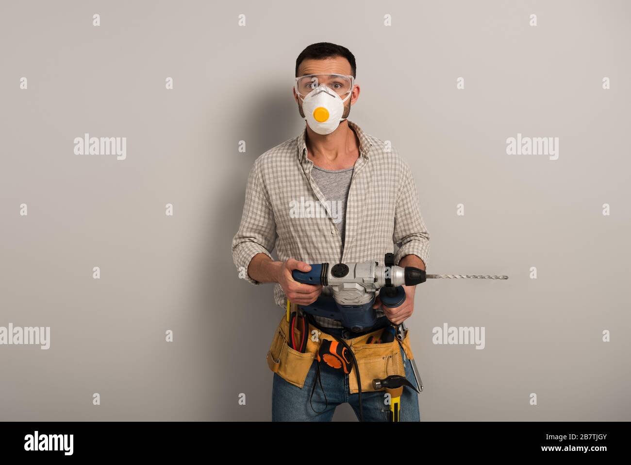 workman in safety mask holding electric drill on grey Stock Photo - Alamy