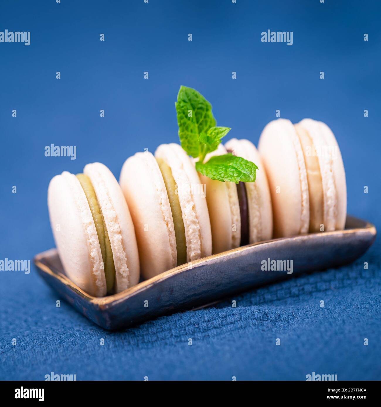 Homemade vanilla macaroons or macarons with mint leaf on a classic blue ...