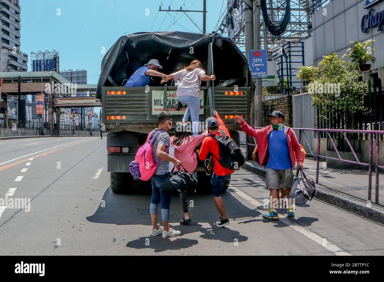 Makati City. 18th Mar, 2020. People climb up a military truck offering ...