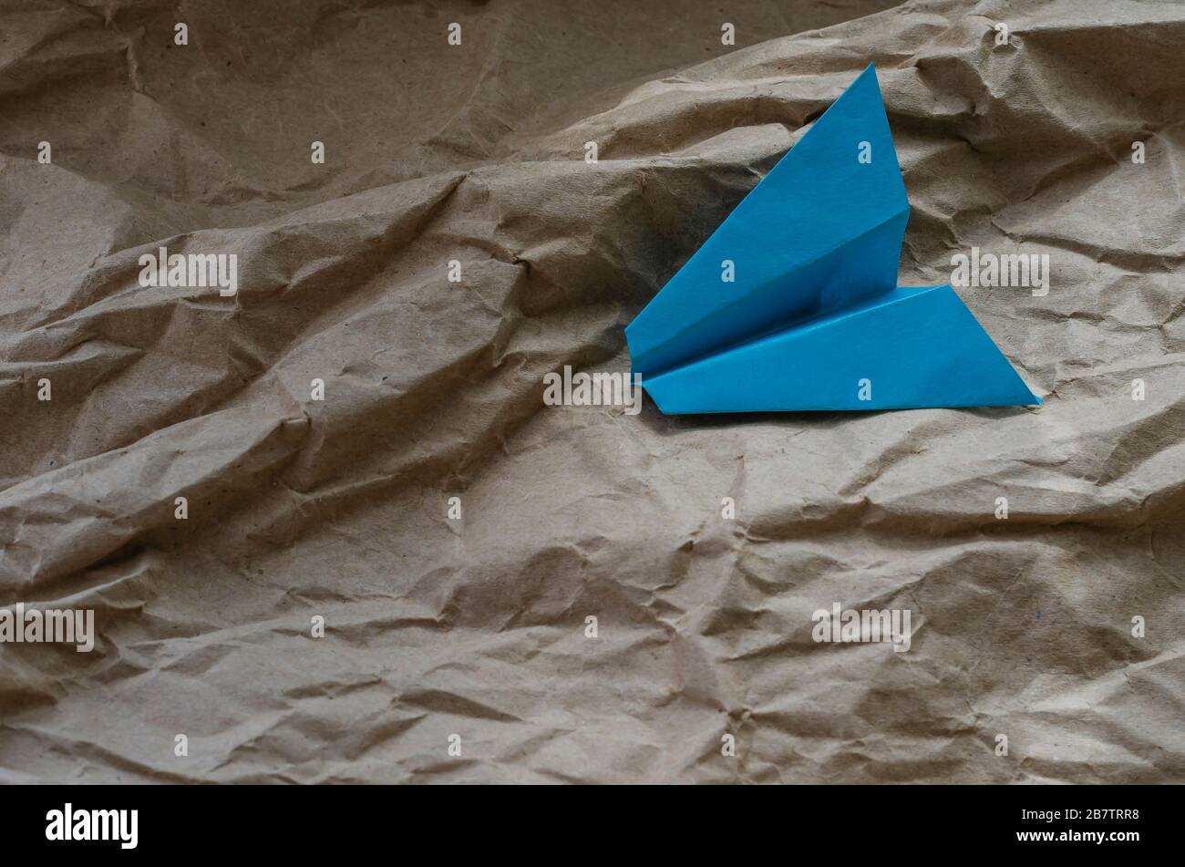 Single blue paper plane on a beige background. Crumpled wrapping paper ...