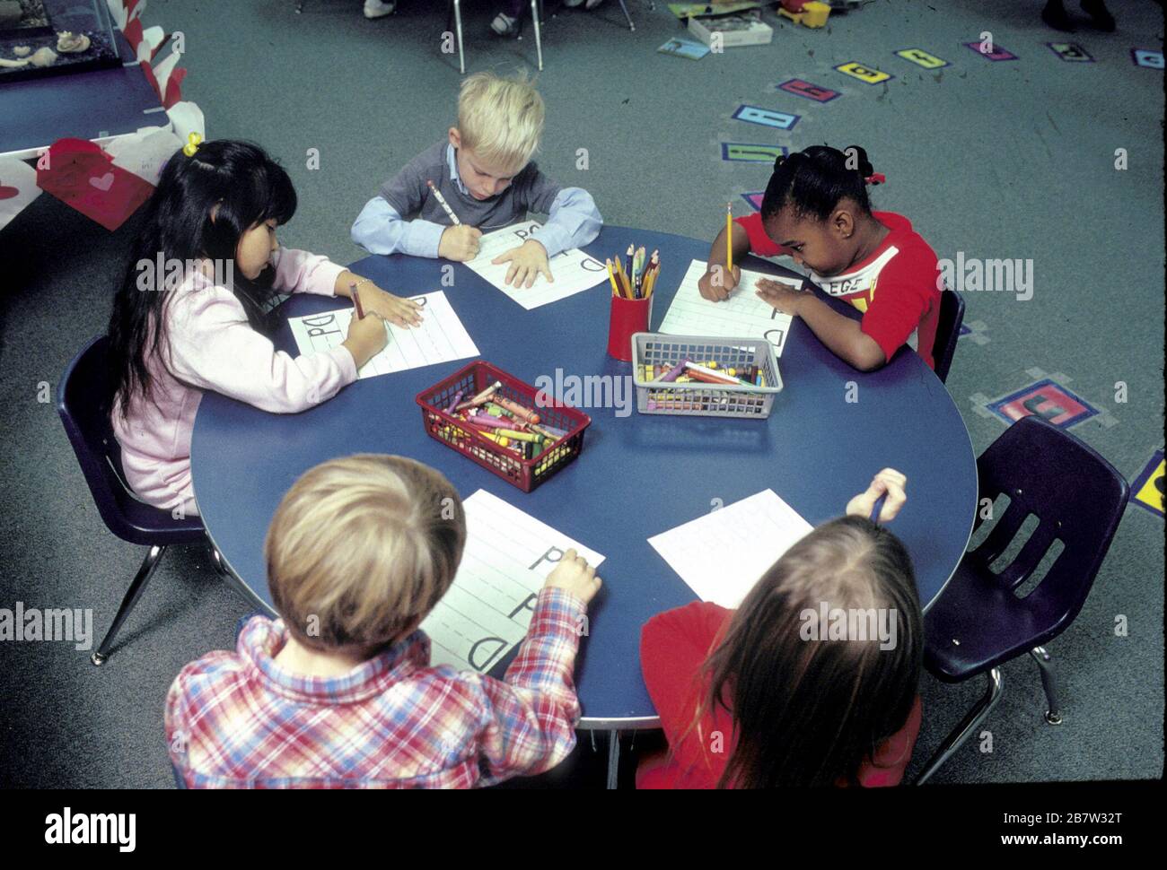 Kindergarten students sitting at table practice writing alphabet ...