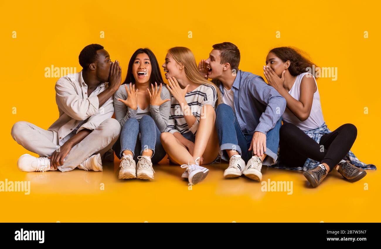 Group of multiracial friends sharing gossips over yellow background ...