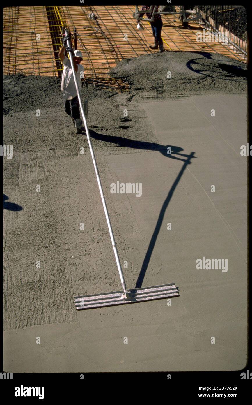Construction worker smooths freshly poured concrete using along-handled ...