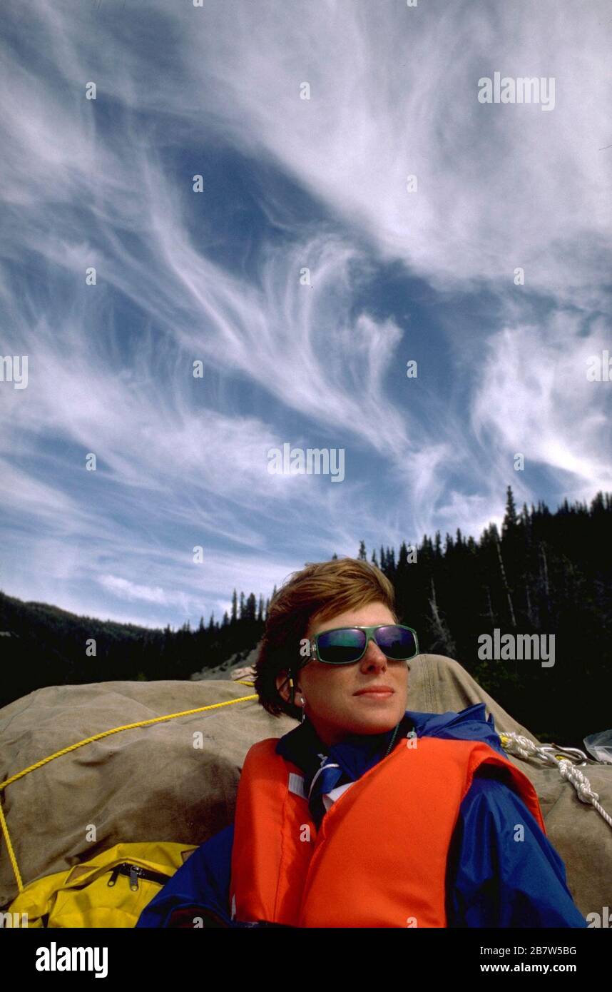 Woman wearing lifejacket and sunglasses leans against gear lashed into ...