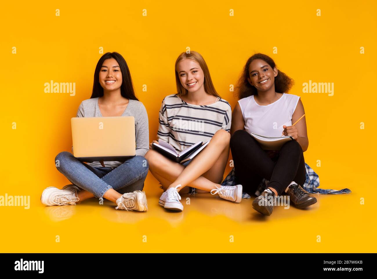 Three students girls studying together, using laptop over yellow ...