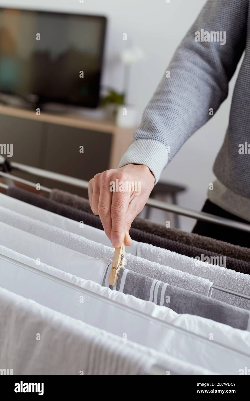 closeup of a young caucasian man hanging wet clothes on a drying rack ...