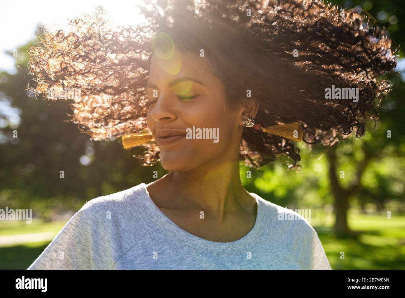 Smiling woman twirling her curly hair outside in a park Stock Photo - Alamy