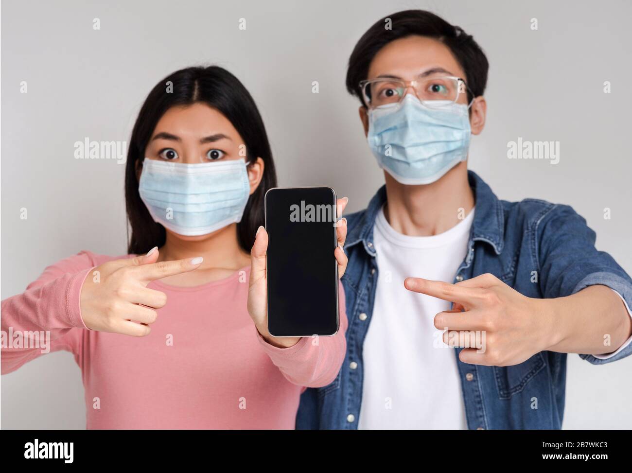 Asian Couple In Medical Masks Pointing At Smartphone With Black Screen ...