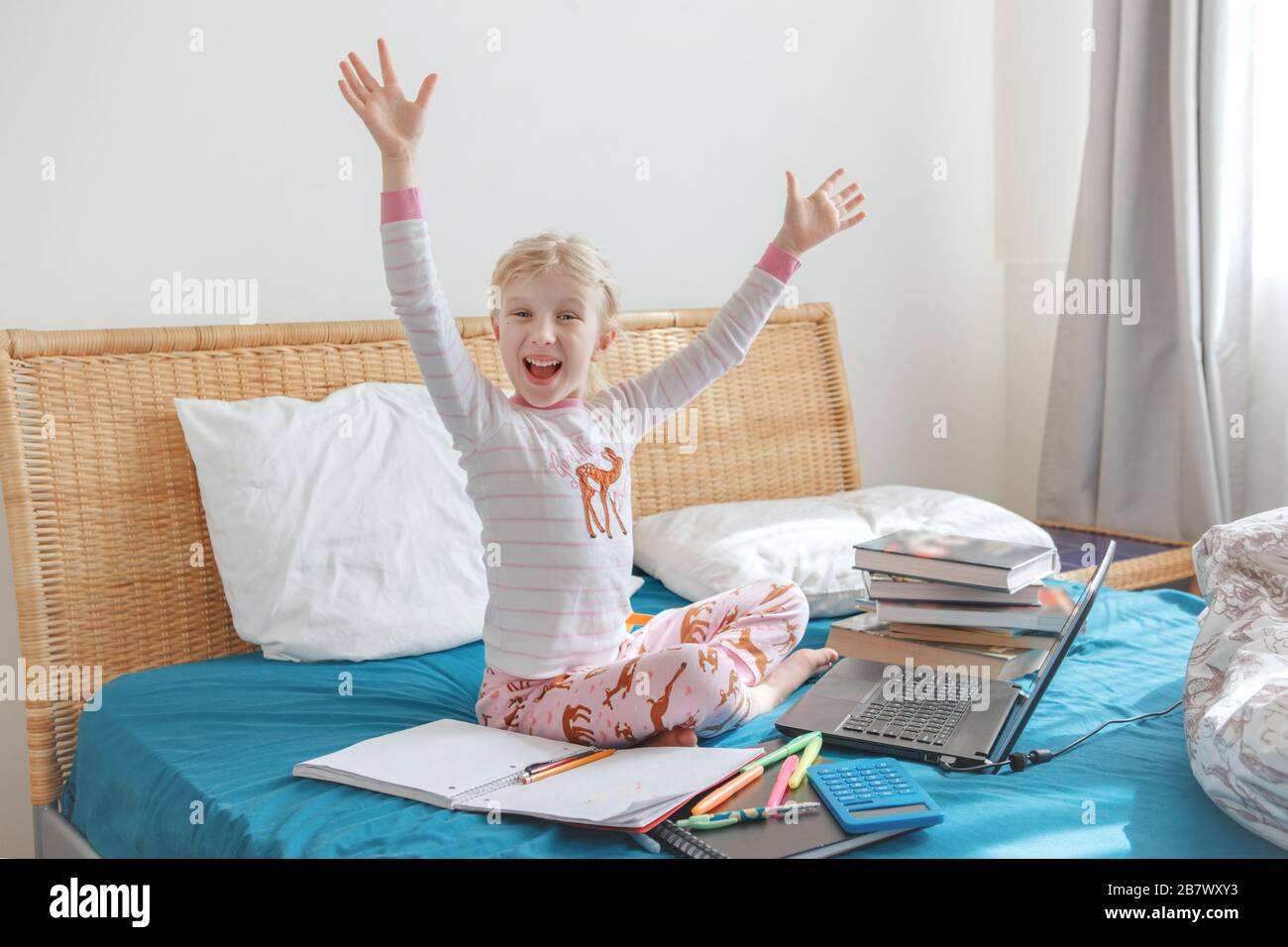 Happy Caucasian girl child sitting in bed learning online on Internet ...