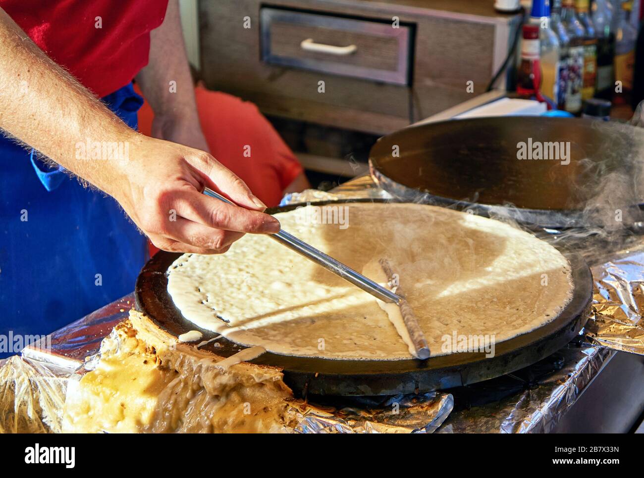 Making crepes pancakes at a market. A hand makes crepes on a metal ...