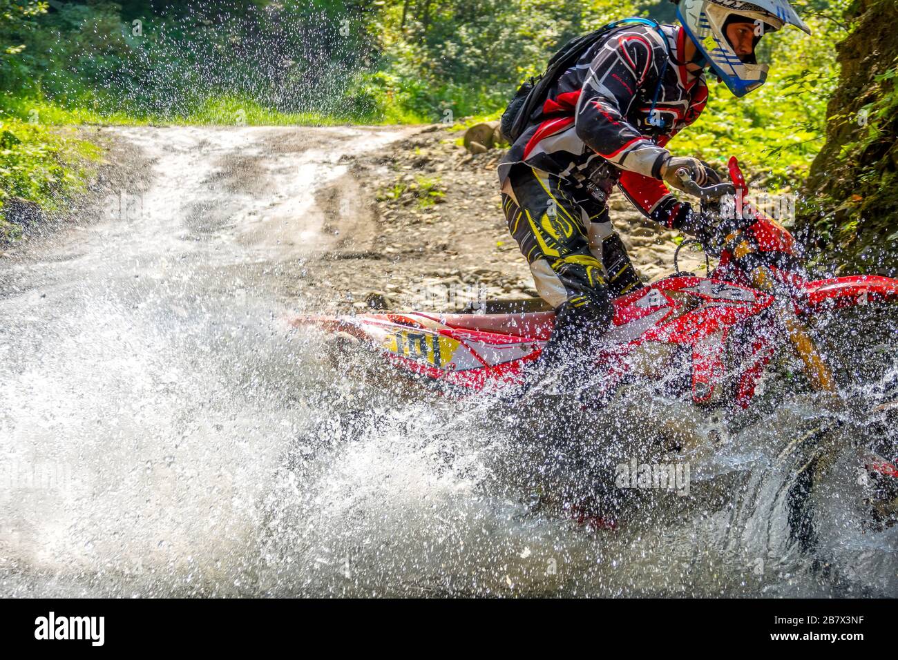 Summer day. A lot of splash of water hides an enduro motorcycle when an ...