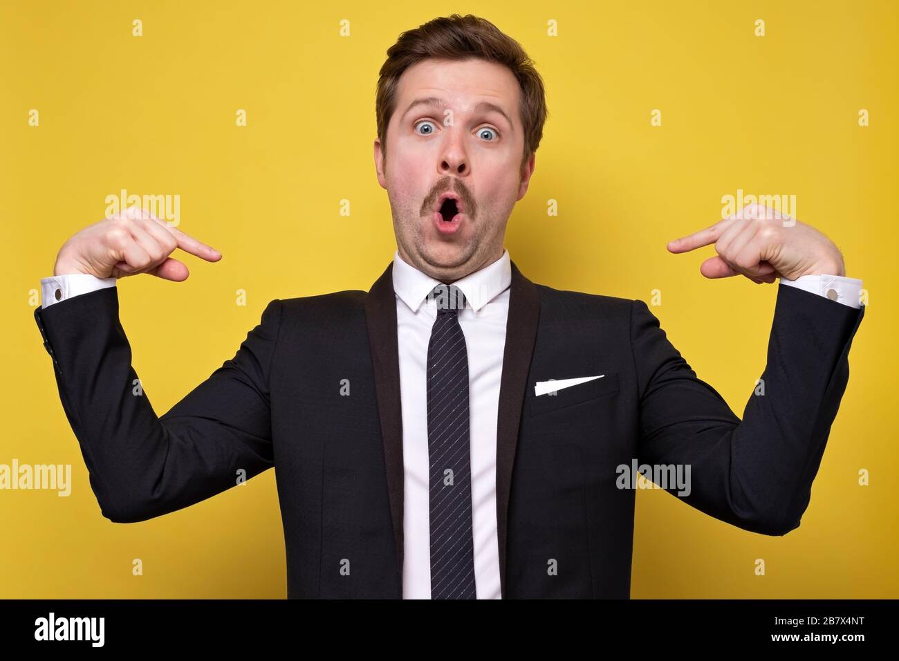Positive young man with mustache smiling and pointing at himself with ...