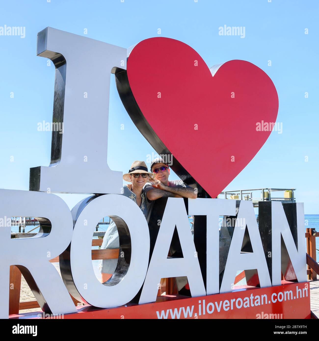 Happy couple standing behind "I Love Roatan" sign, West End Village ...