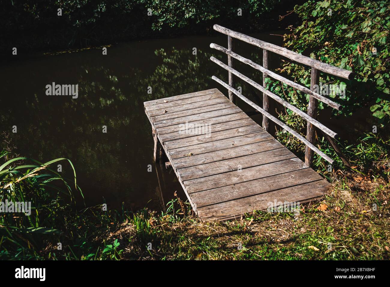 An old brown wooden dock bridge with hand railings on top of a small ...