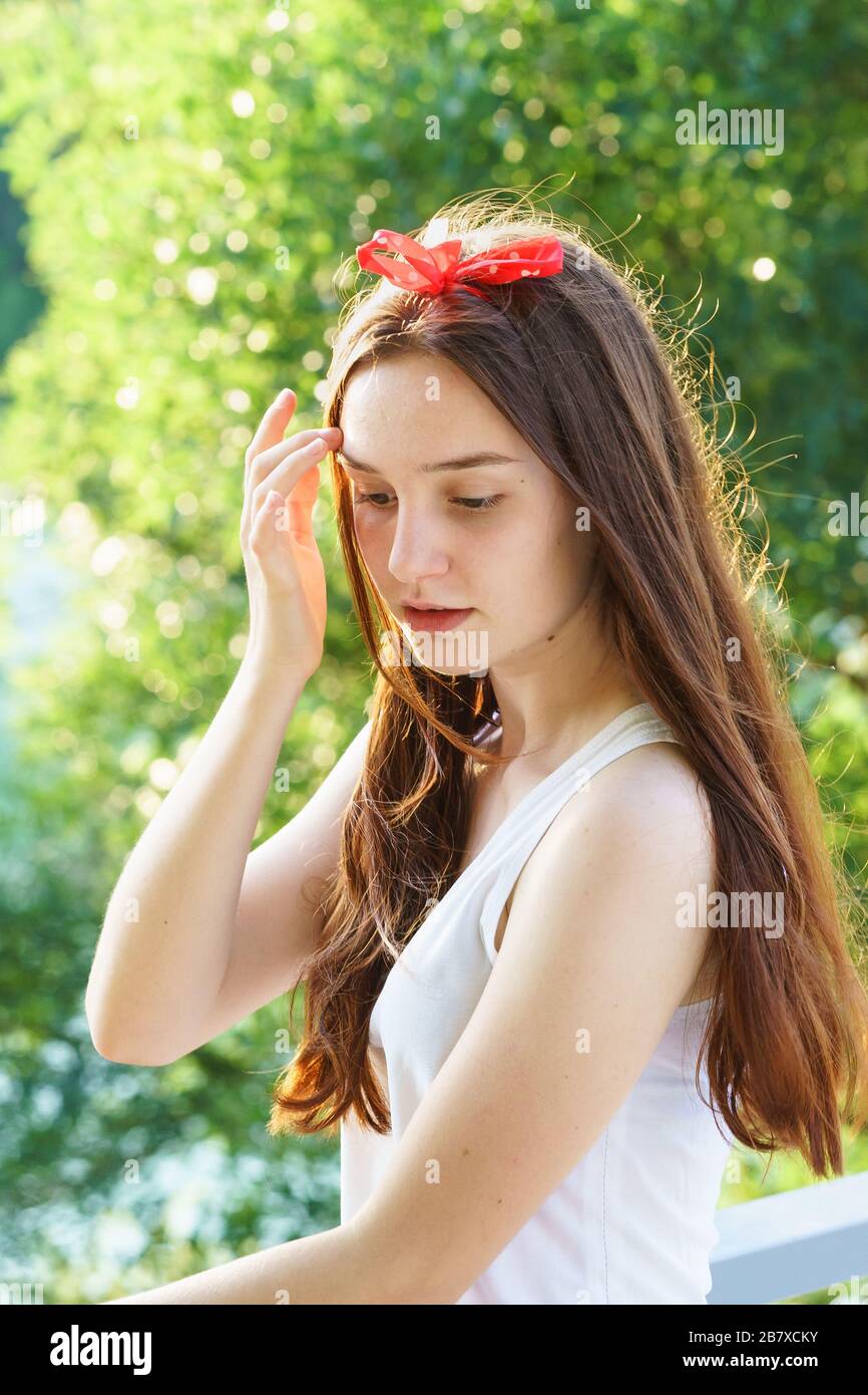 A brooding sad teenage girl in a white blouse is standing on the street ...