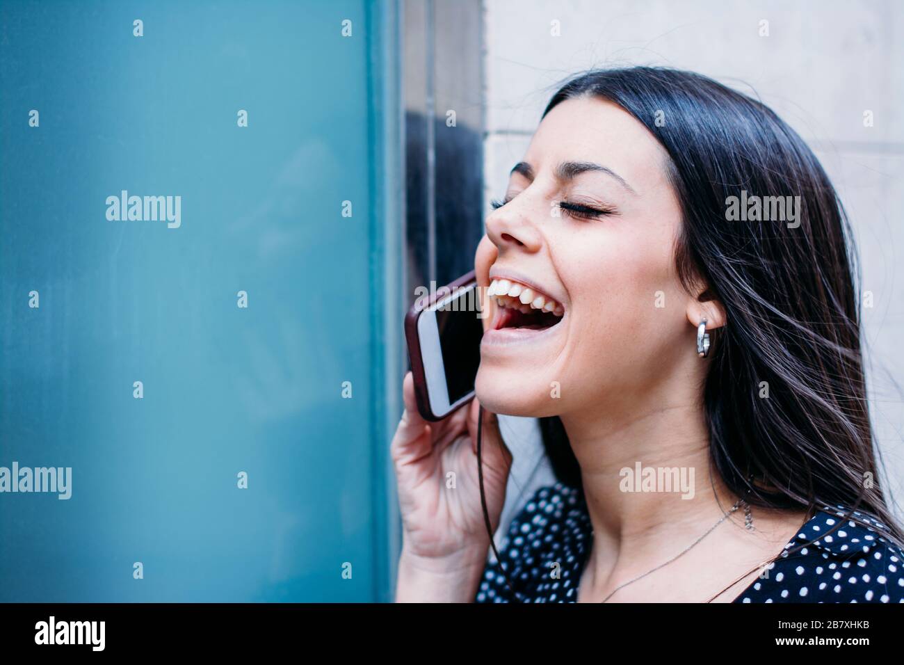 Modern and smiling young girl talking on her mobile phone next to her ...