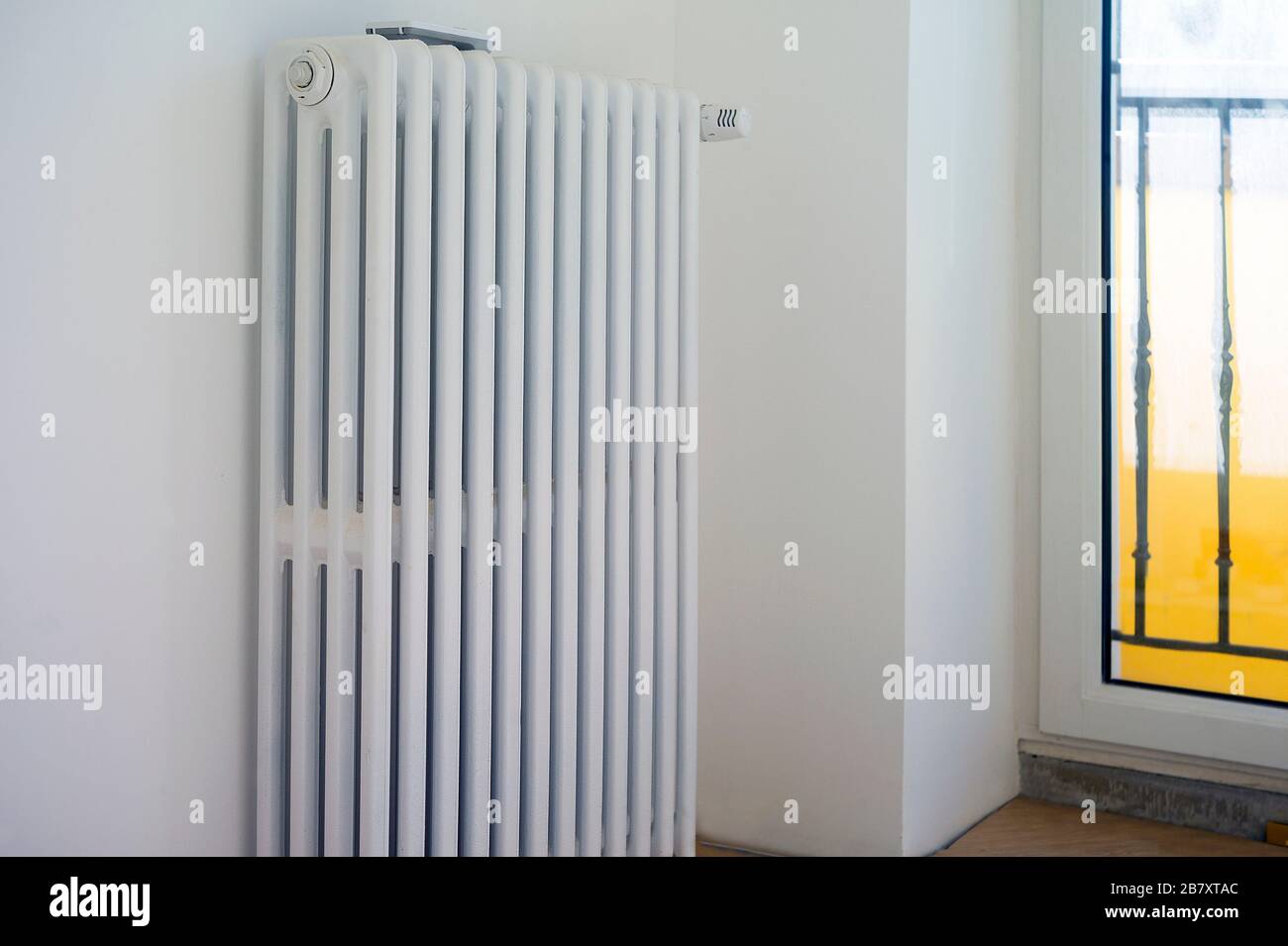 A radiator hanging on the wall next to a balcony door, sunny day shot ...