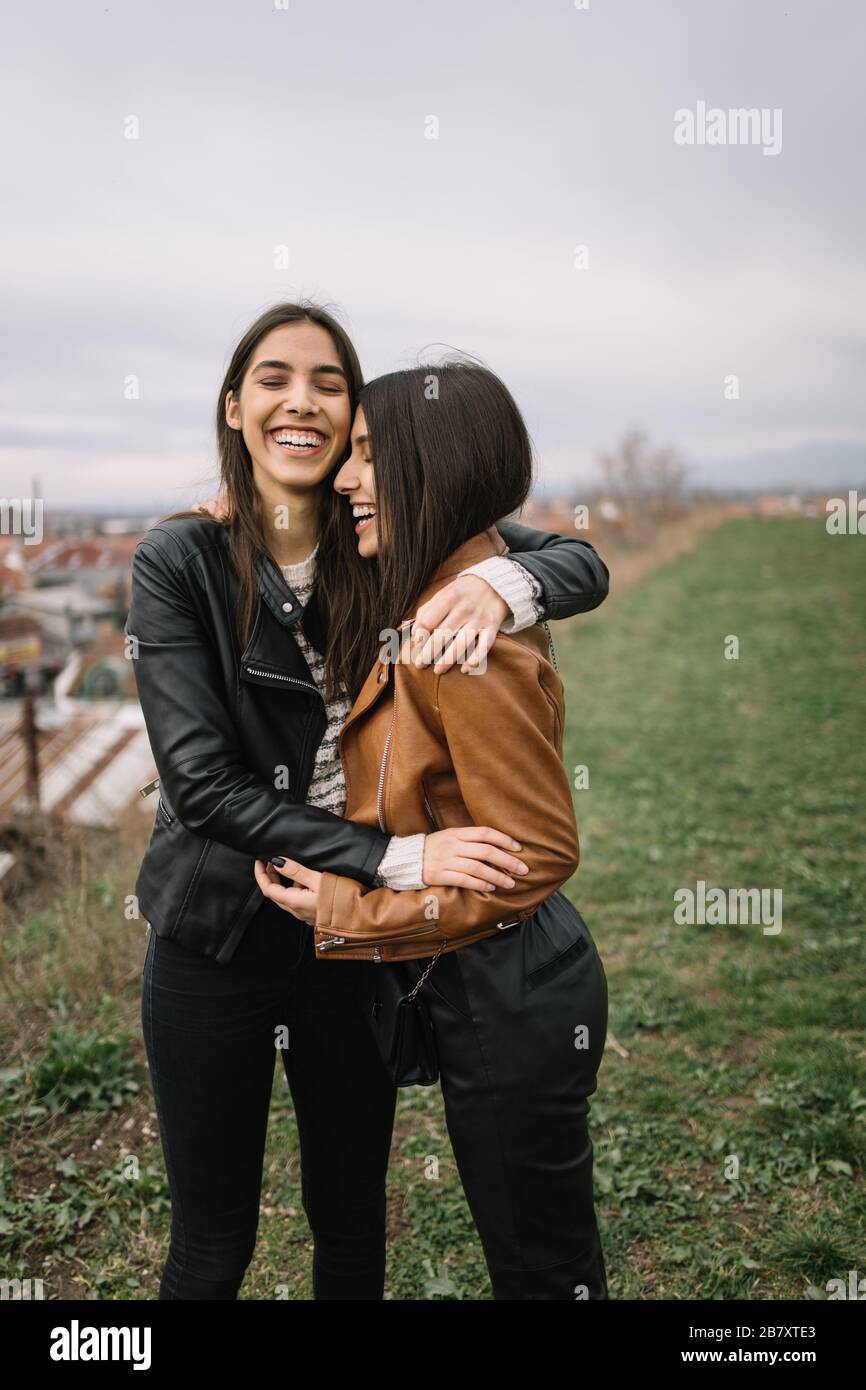 Two smiling girls cuddling while standing on field Stock Photo - Alamy