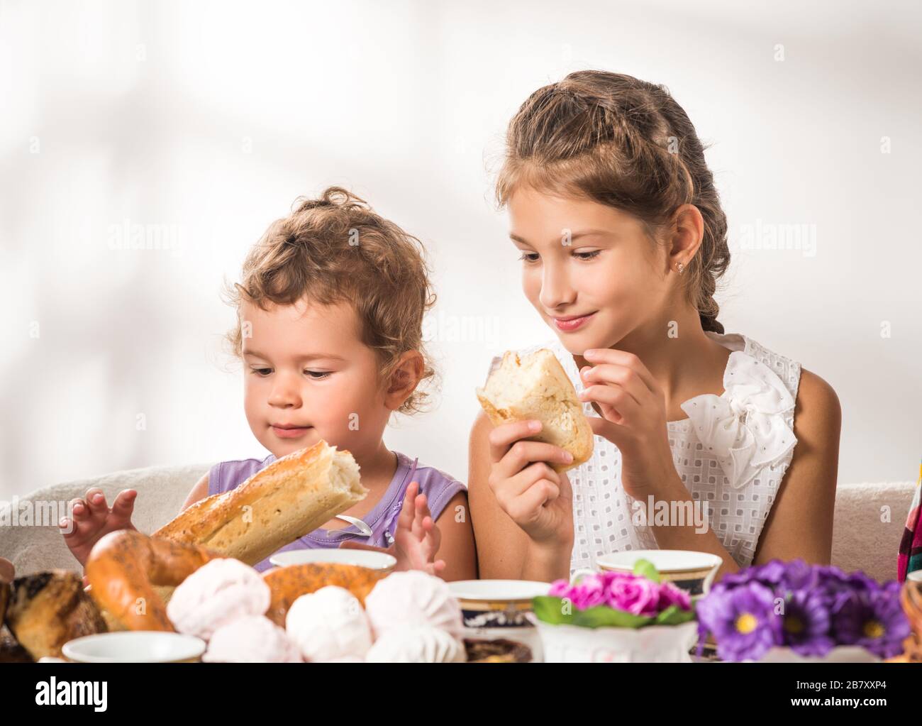Funny little children eat fresh bread and rolls during breakfast ...