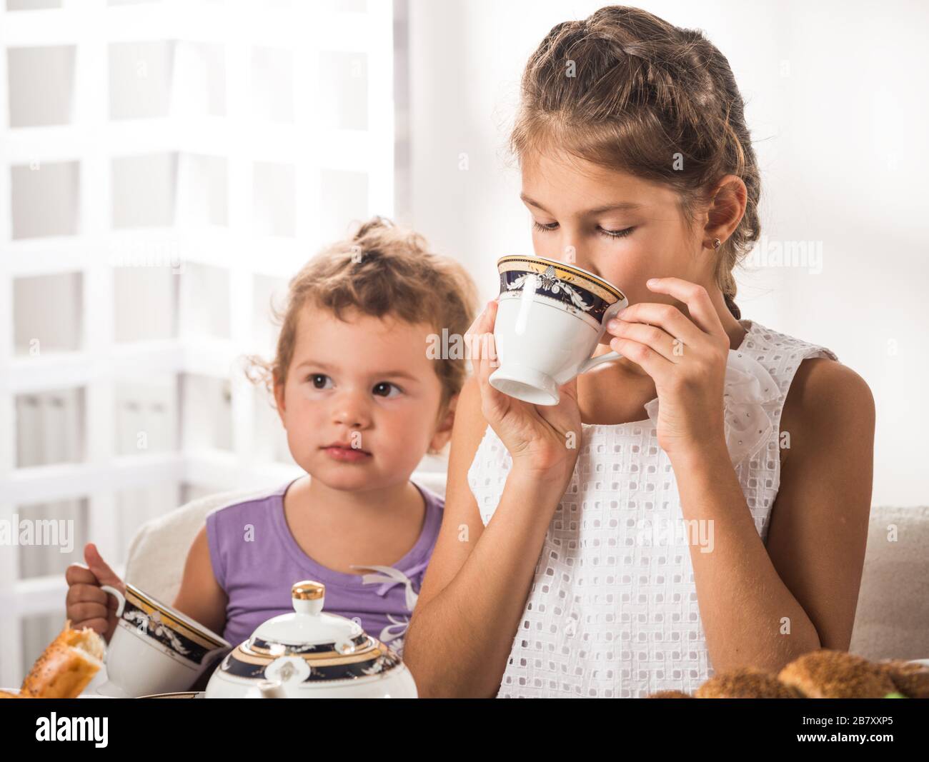 Three little cute Russian children drink tea and eat rolls and ...