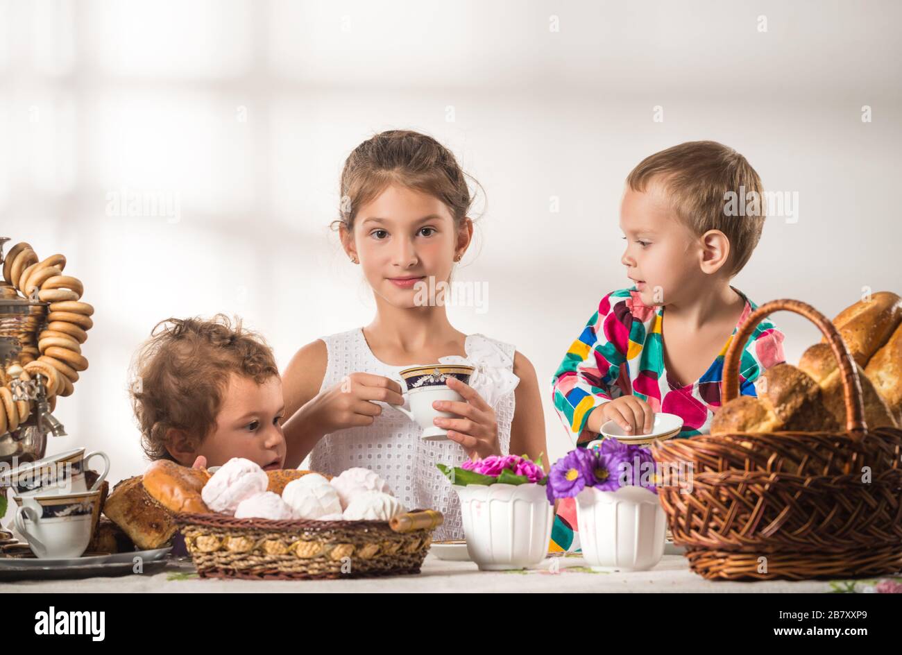 Three little cute Russian children drink tea and eat rolls and ...
