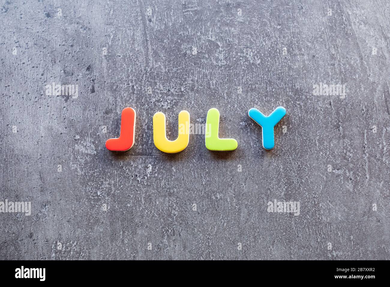 July word written with colorful letters on grey granite stone ...