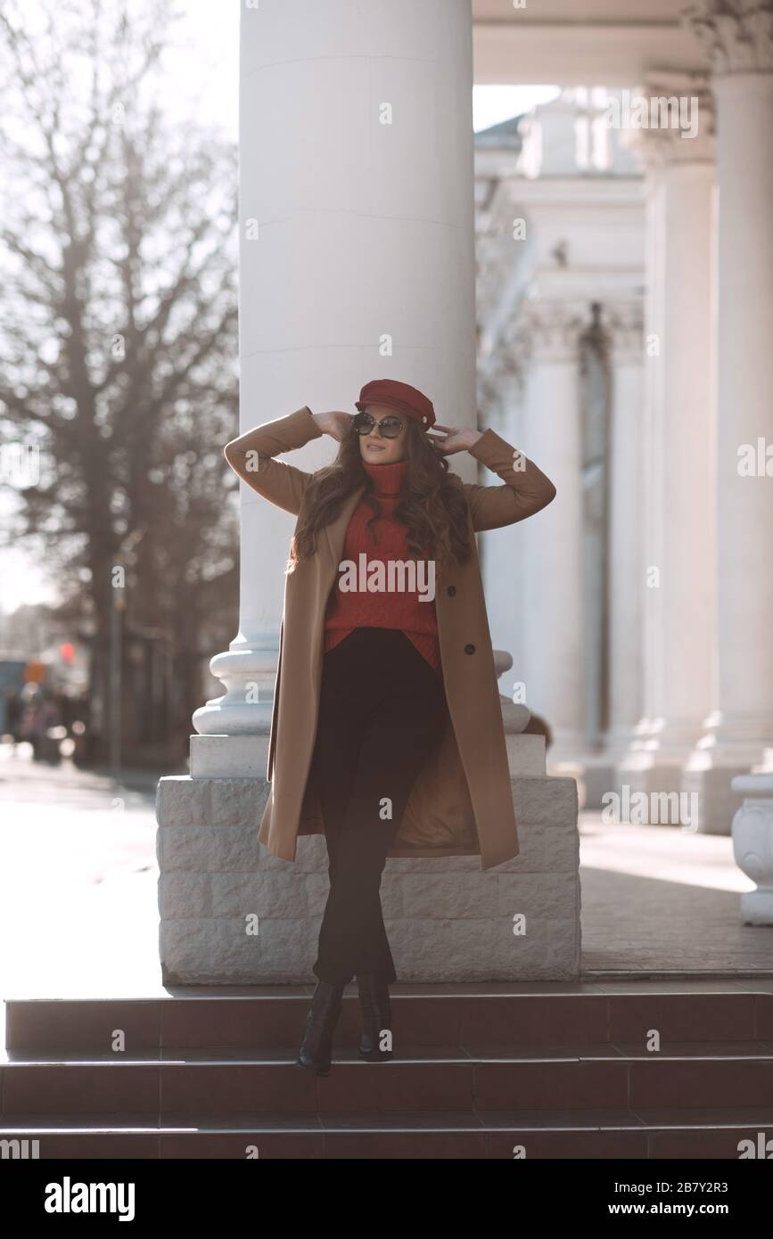 Stylish woman wearing winter coat and hat posing on street over city ...