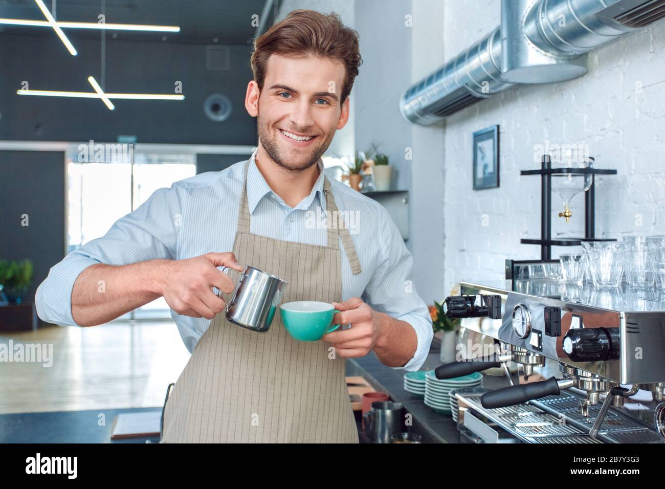 Happy young adult barista in apron uniform working in cafeteria ...