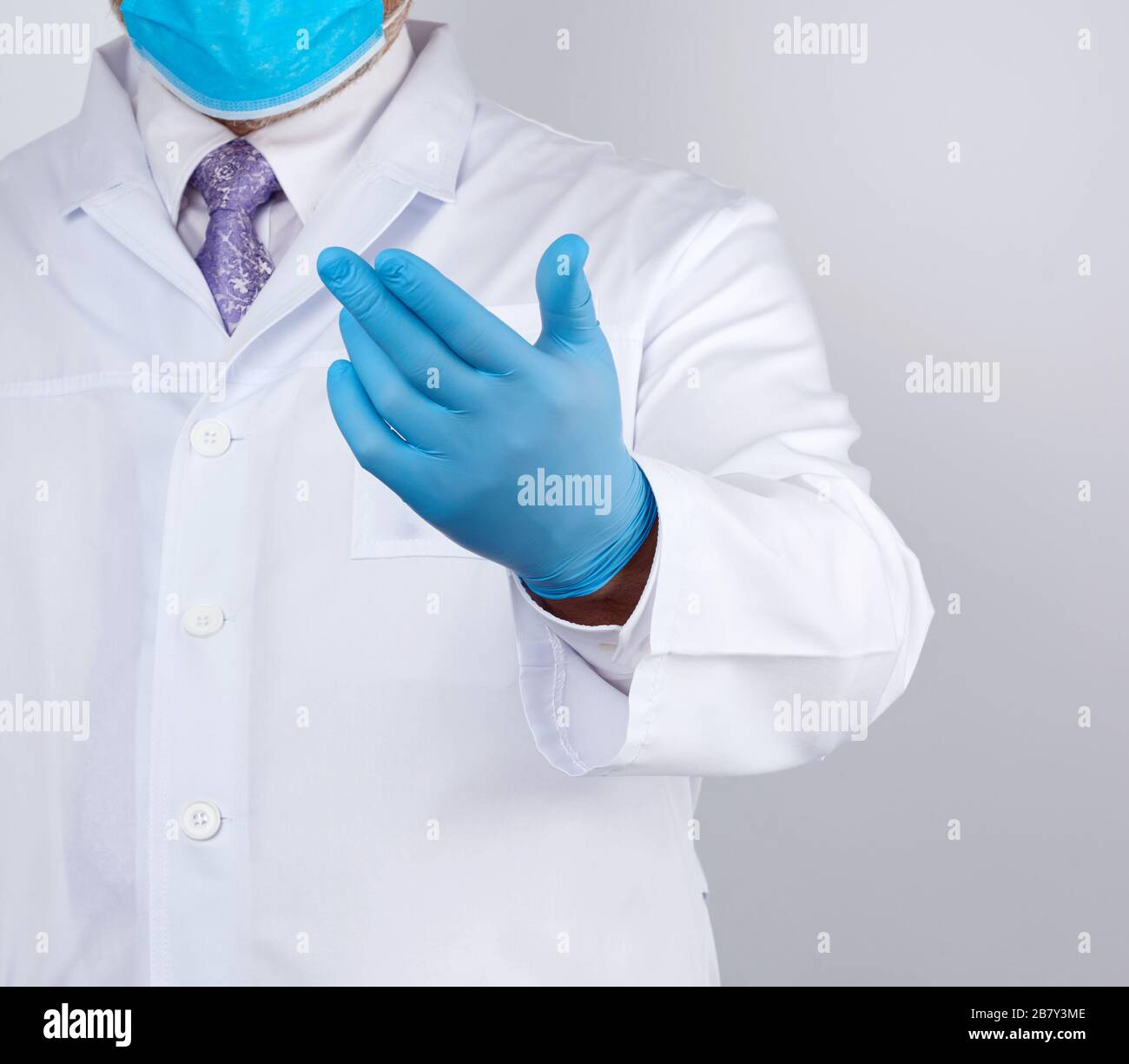 doctor in a white coat with buttons and blue latex gloves holds out his ...