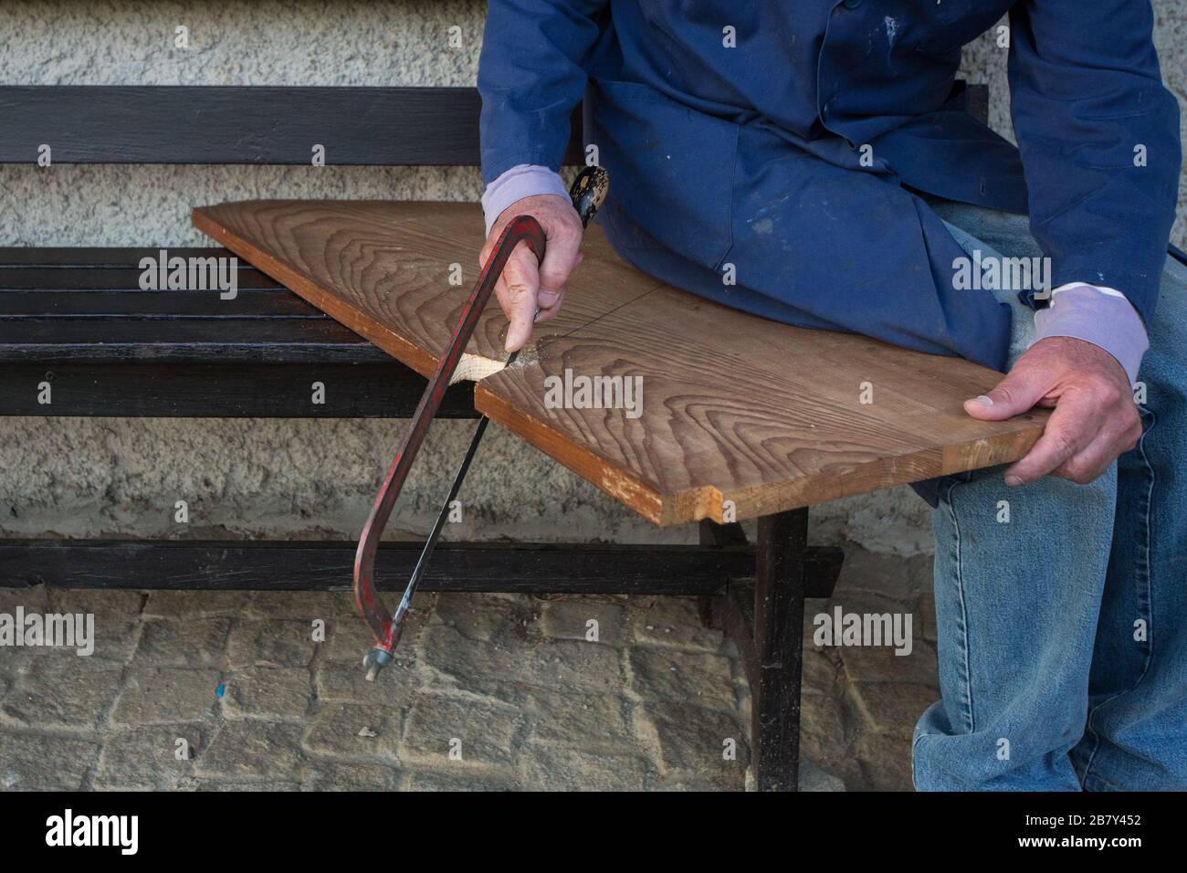 hands of older man working cutting plank with wood handsaw outside on ...