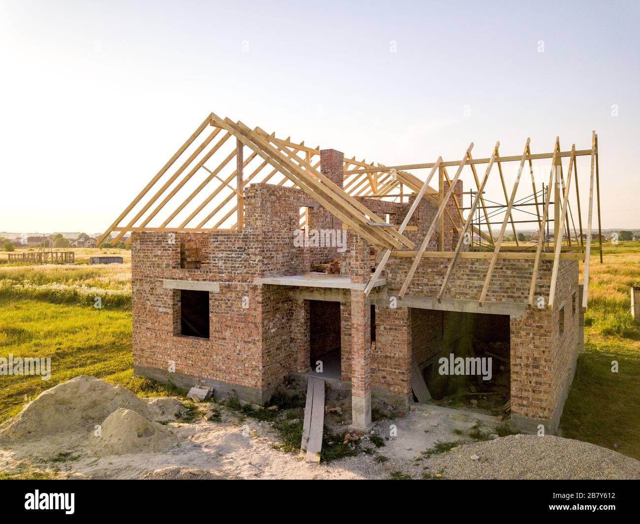Unfinished brick house with wooden roof structure under construction ...