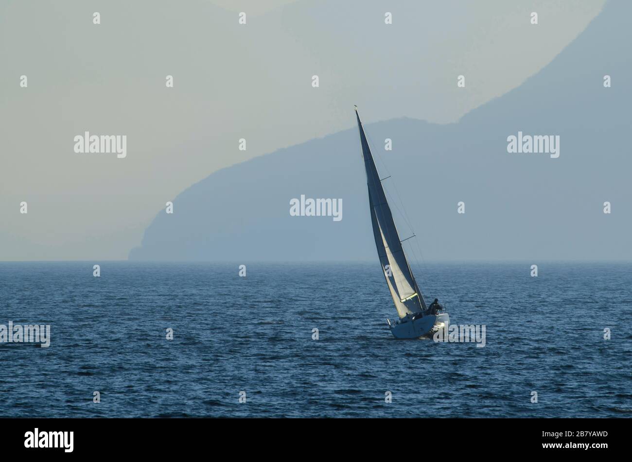 Small sailing ship on the sea surrounded by mountains covered in the ...