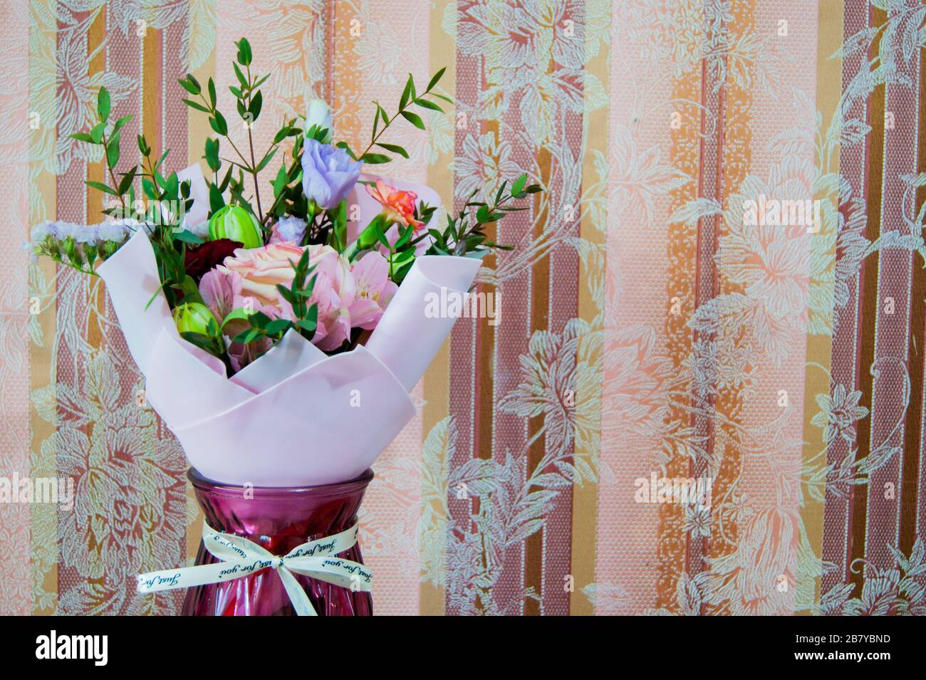 A delicate bouquet of different flowers in a light pink wrapper stands ...