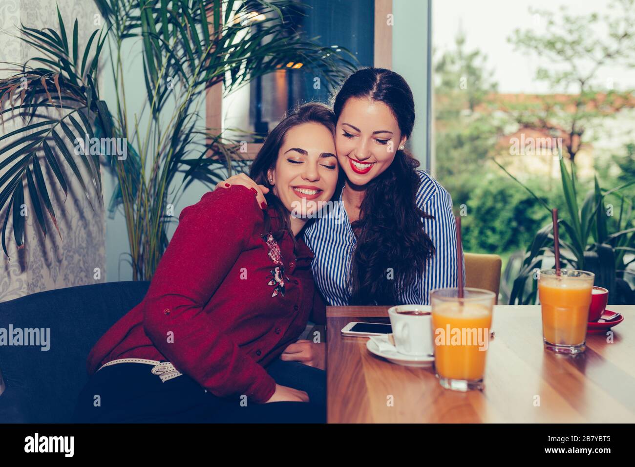 Happy young woman hugging her best friend, sitting in a cafe, having ...