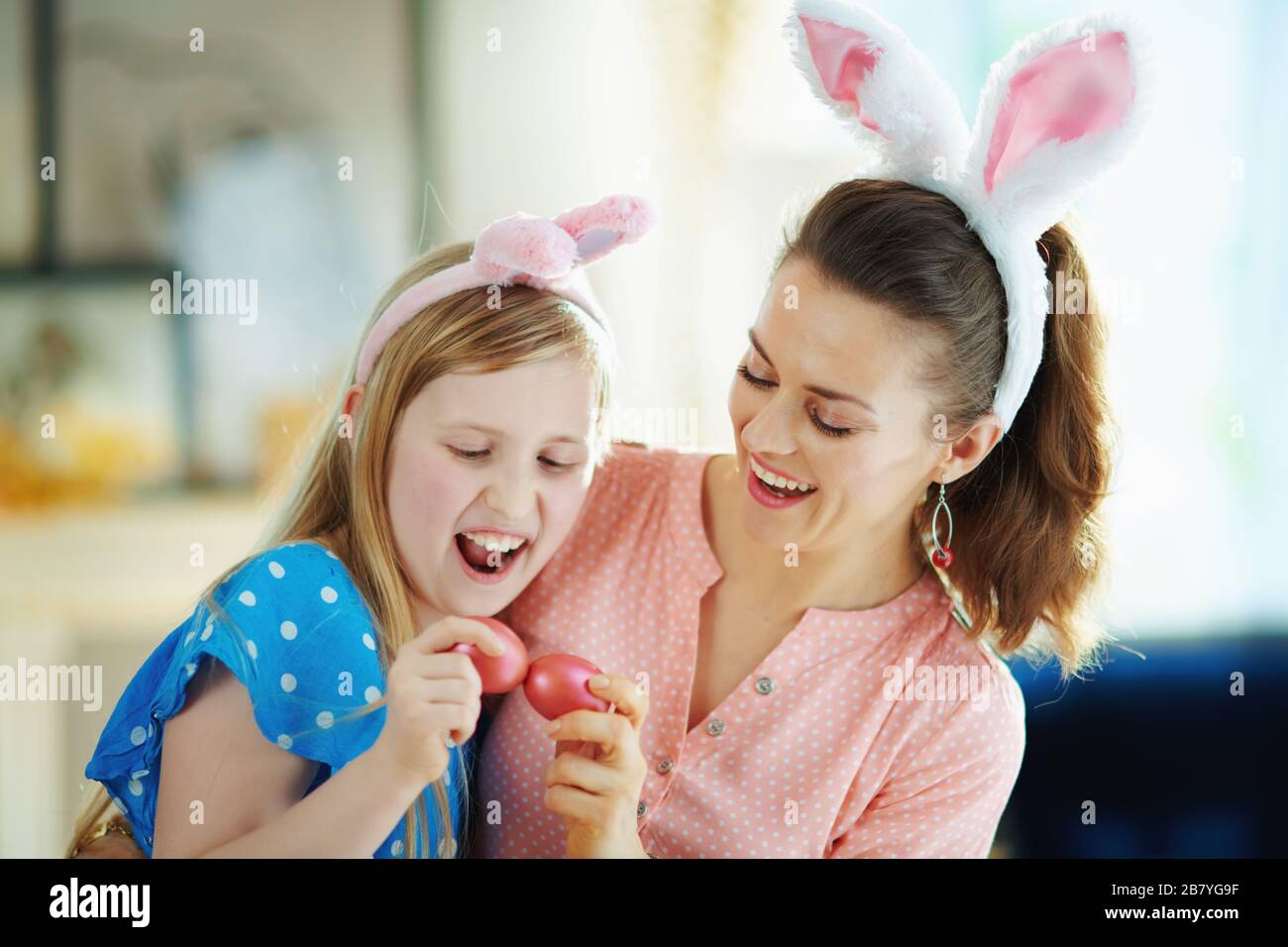cheerful modern mother and child in easter bunny ears having egg ...