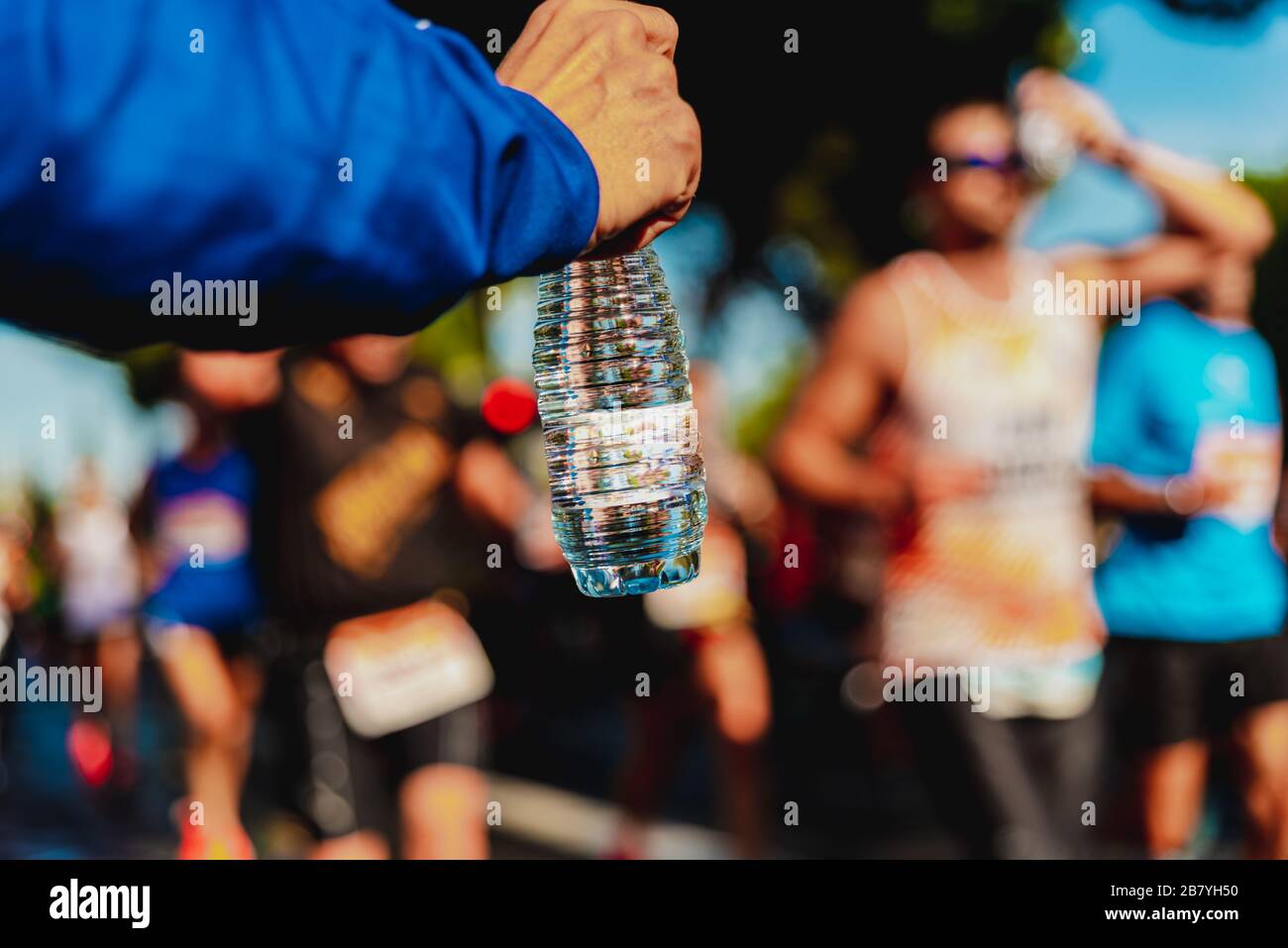 A helping hand delivers a bottle of water to a runner in a running race ...
