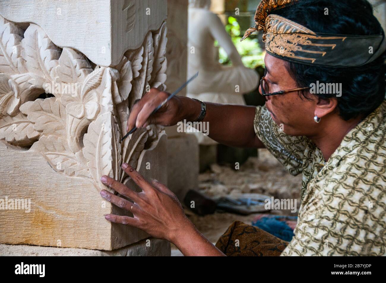 A Balinese artisan hard at work sculpting a statue out of a block of ...