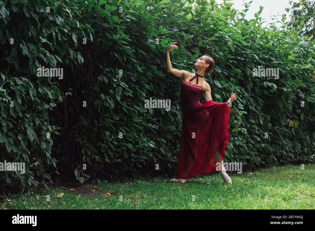 Woman ballerina in red ballet dress dancing in pointe shoes posing next ...
