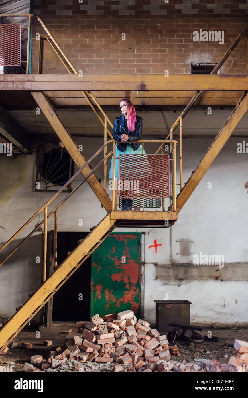 Portrait of a young girl with pink hair standing on the rusty stairs ...