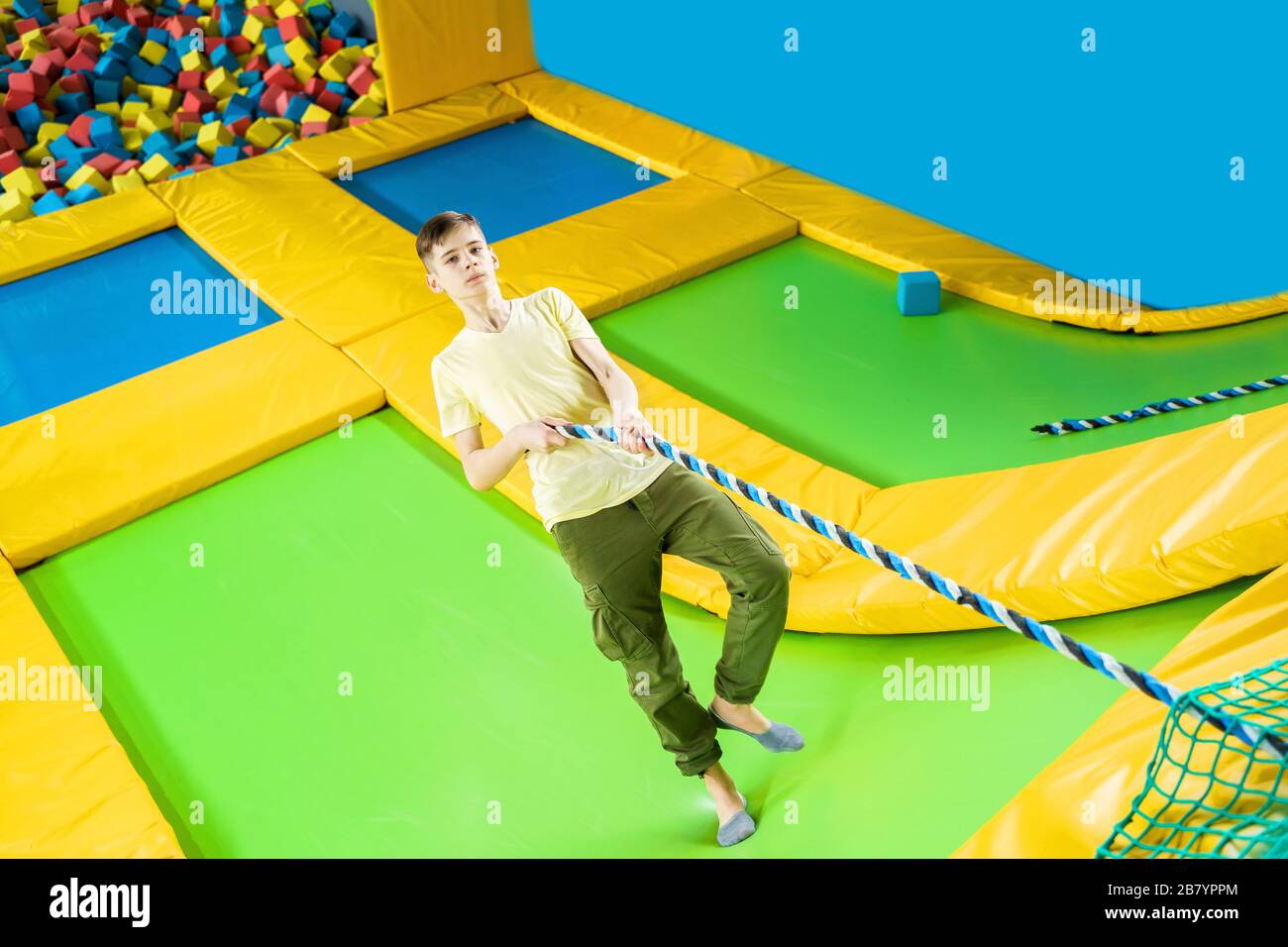 Teenage boy playing in trampoline center jumping and climbing with rope ...