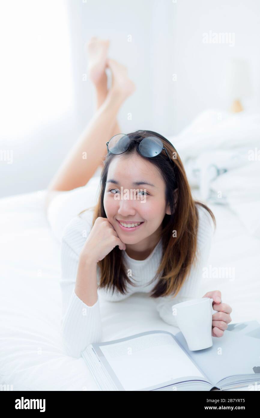 charming woman lying on bed reading a book and holding coffee cup ...