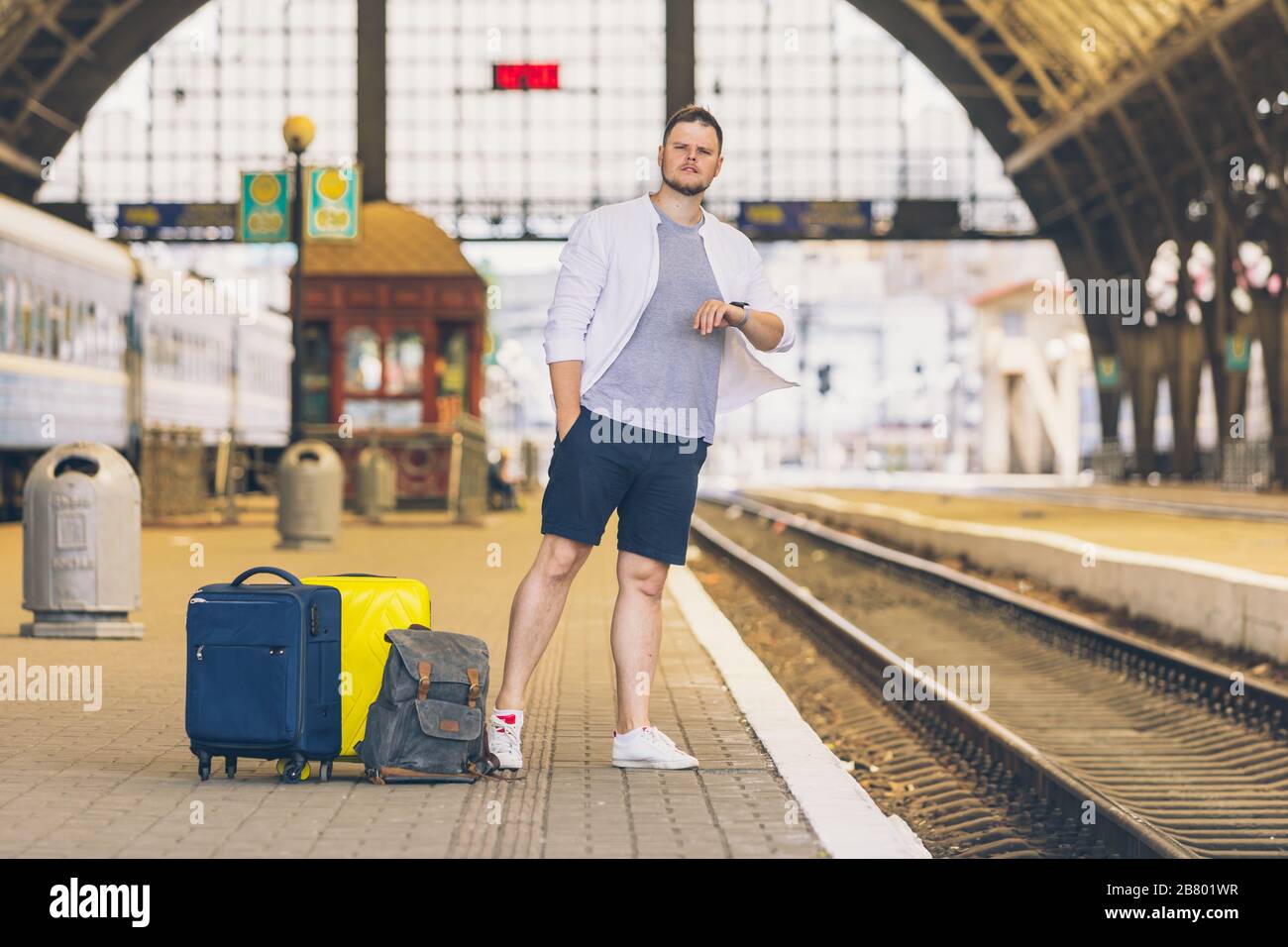 man at railway station waiting for late train with bag looking at watch ...