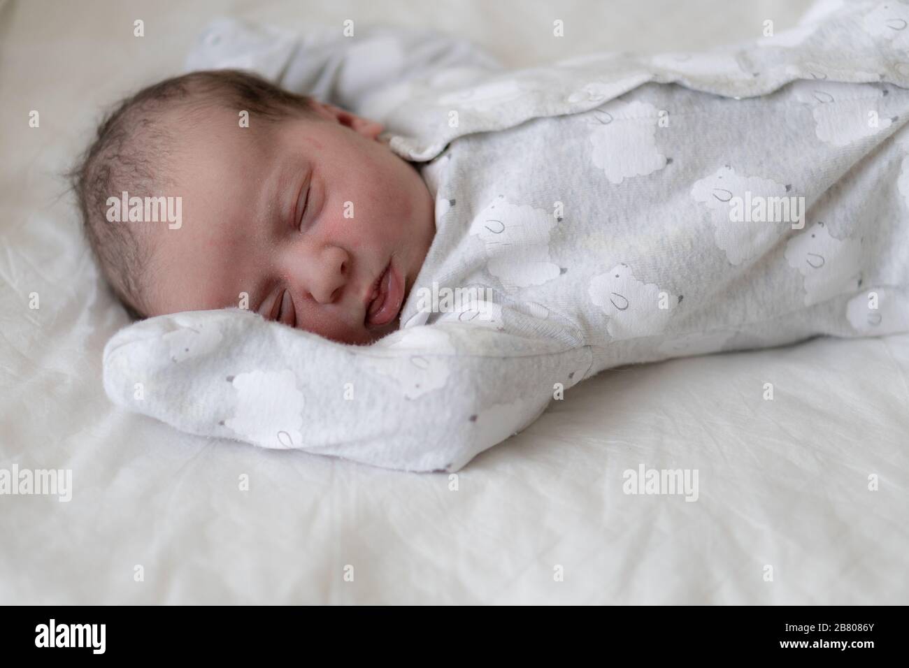 A newborn baby lies on its back with closed eyes and shows its tongue ...