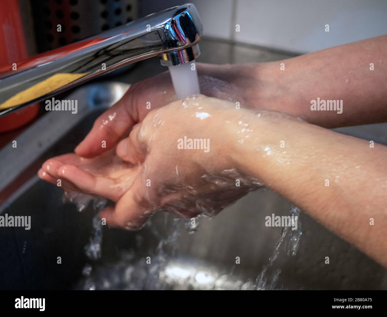 A female thoroughly washes her hands at a kitchen sink. She firsts uses ...